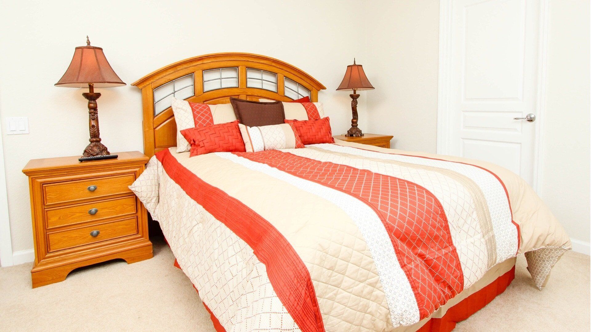 Quarto com cama de madeira, duas mesas de cabeceira, cômoda de madeira e uma porta.