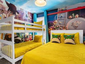 Quarto infantil com beliches e um mural de personagens animados.