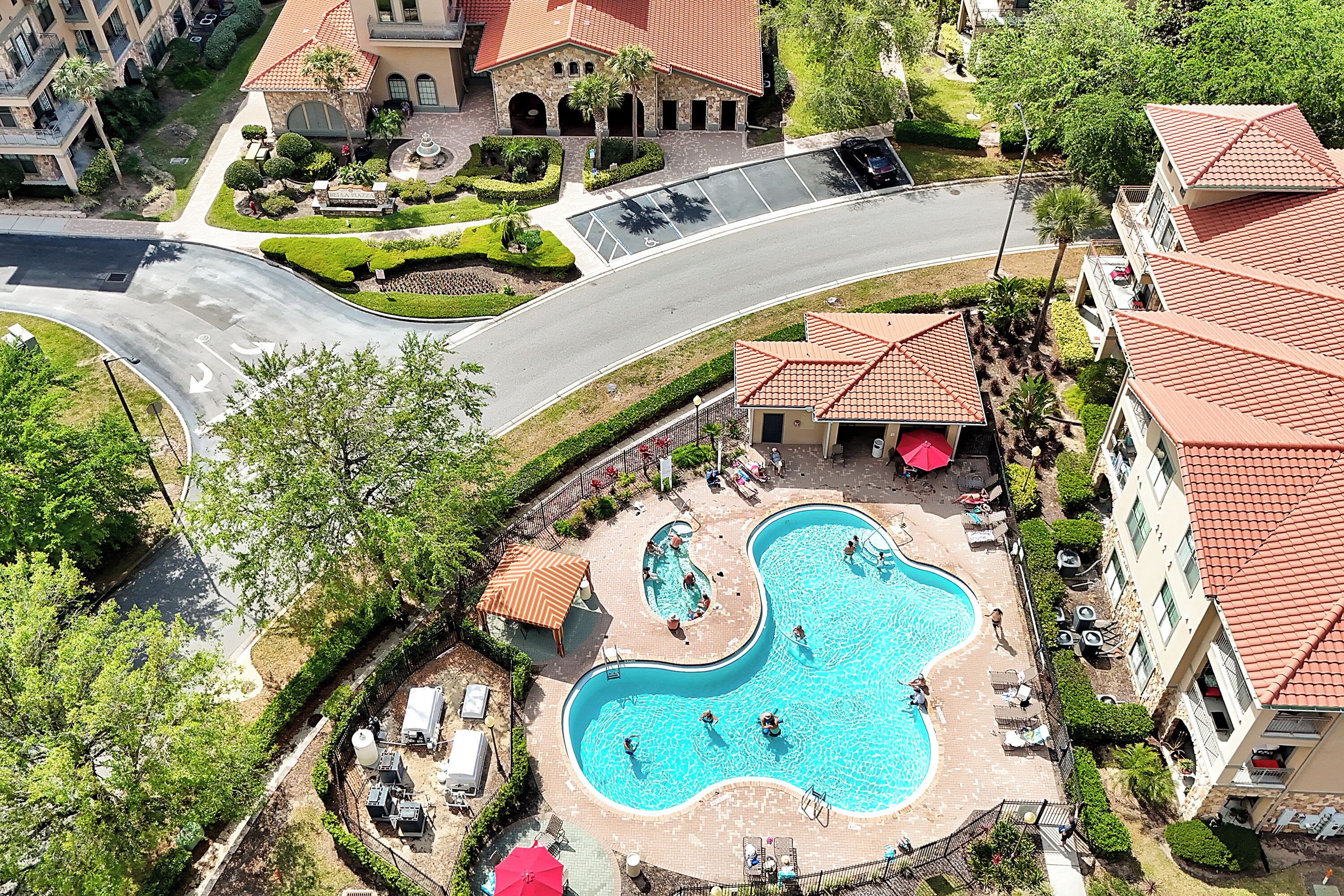 Vista aérea de um resort com piscina, jardins bem cuidados e área de estacionamento.