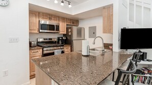 Uma cozinha moderna com bancadas de granito, eletrodomésticos de aço inoxidável, armários de madeira e uma TV embutida.