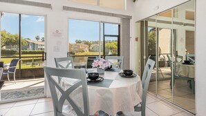 Uma sala de jantar com mesa posta para quatro pessoas, janelas amplas e vista para o exterior.