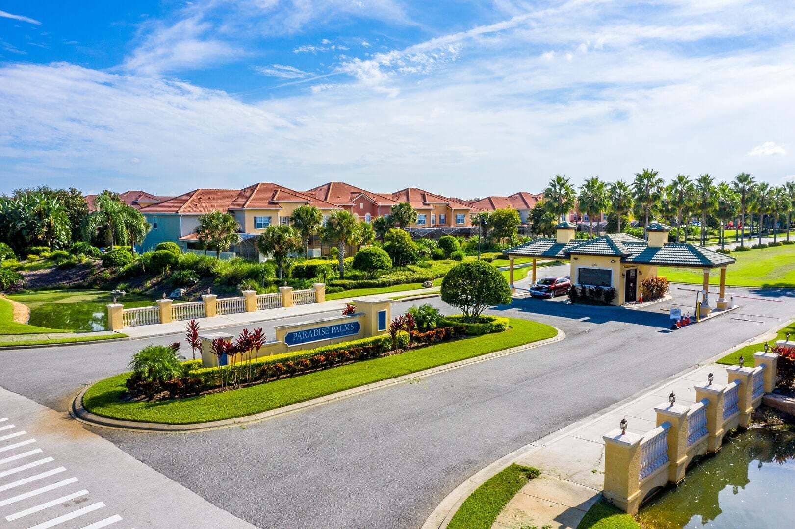 Condomínio fechado com uma estrada central, um pequeno edifício com a inscrição 'Paradise Palms' e um espelho d'água.