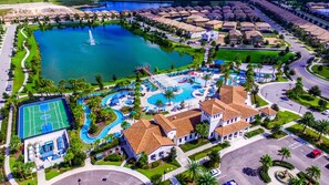 Vista aérea de um resort com uma piscina grande, quadras de tênis e uma fonte.