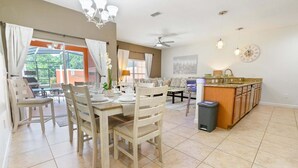 Uma área de refeições com uma mesa posta para quatro, cozinha com pia e armários, e um ventilador de teto.