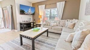 Uma sala de estar com sofá, mesa de centro, televisão e um quadro de um castelo.