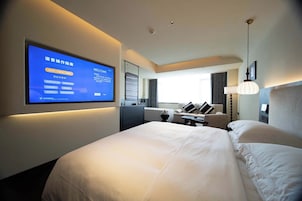 Quarto de hotel moderno com uma cama grande, televisão na parede, uma escrivaninha e janela com cortinas.