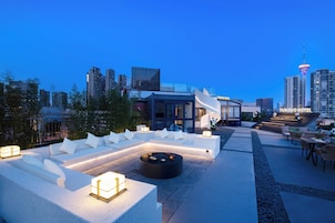 Área de lounge no terraço com assentos, lareira e vista para o horizonte urbano.