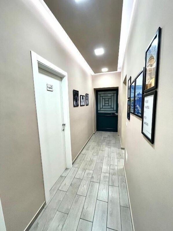 Um corredor com piso de madeira clara, paredes bege e quadros na parede direita.