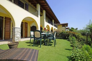 Um pátio com mesa e cadeiras, cercado por um gramado bem cuidado e diversas plantas.