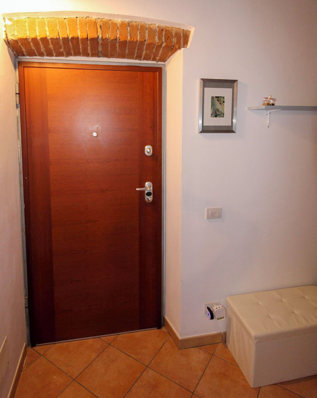 Quarto com porta de madeira, uma pequena estante com um quadro e mesa de cabeceira com um colchão.