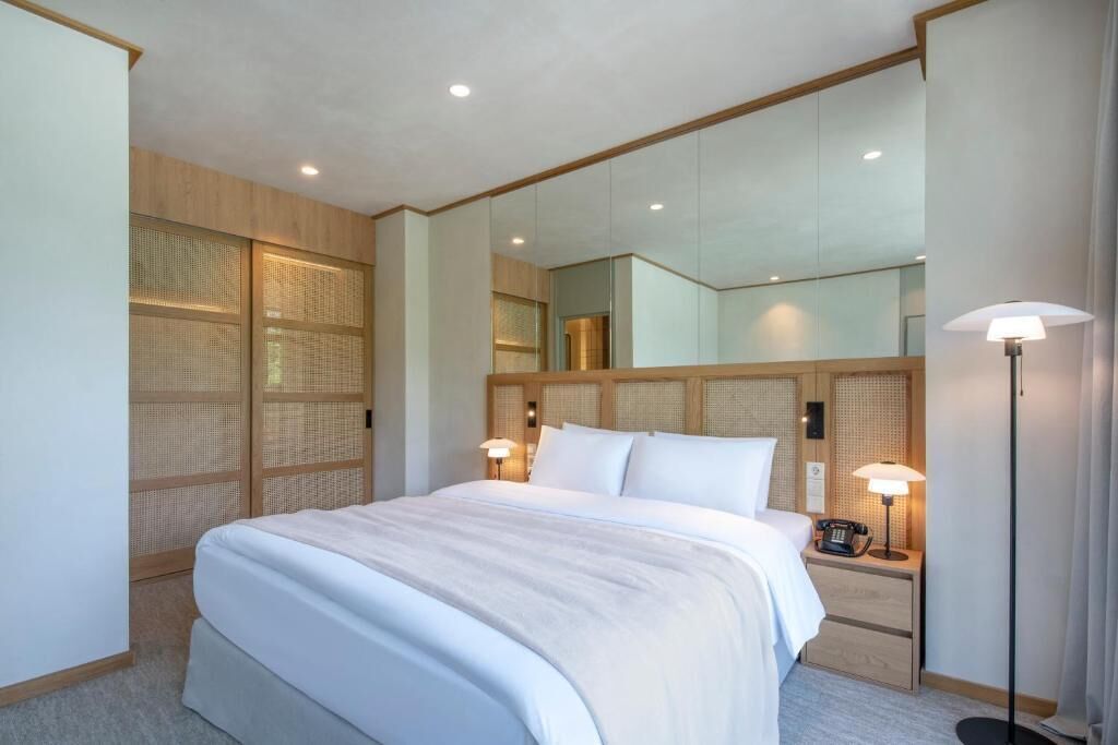 Quarto de hotel com uma cama grande, luminárias de cabeceira, telefone e espelho na parede.