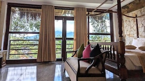 Quarto com cama de dossel, um banquinho com almofadas e janelas amplas com cortinas.