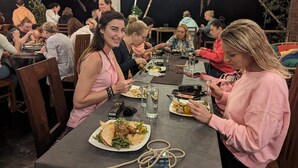 Um grupo de pessoas jantando em um restaurante ao ar livre com telhado de palha e luminárias penduradas.