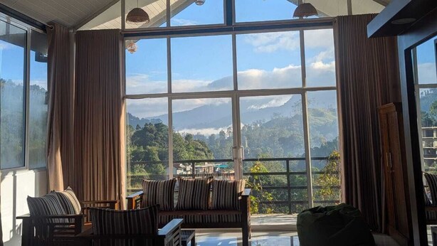 Quarto com amplas janelas proporcionando vista para as montanhas, um sofá e uma cadeira.