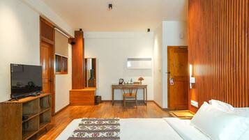 Quarto de hotel com cama, televisão, secretária com cadeira e painéis de madeira.