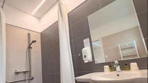 Uma casa de banho moderna com chuveiro, pia e espelho.