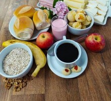 Mesa de café da manhã com diversos alimentos, incluindo pão, maçãs, banana, aveia e uma xícara de café.
