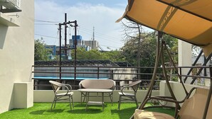 Terraço no topo do prédio com grama sintética, cadeira de balanço, uma mesa e vista para a paisagem urbana.
