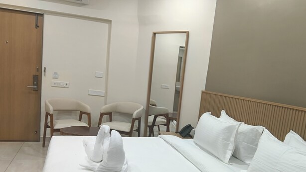 Quarto de hotel com cama bem arrumada, duas cadeiras, um espelho e telefone ao lado da cama.