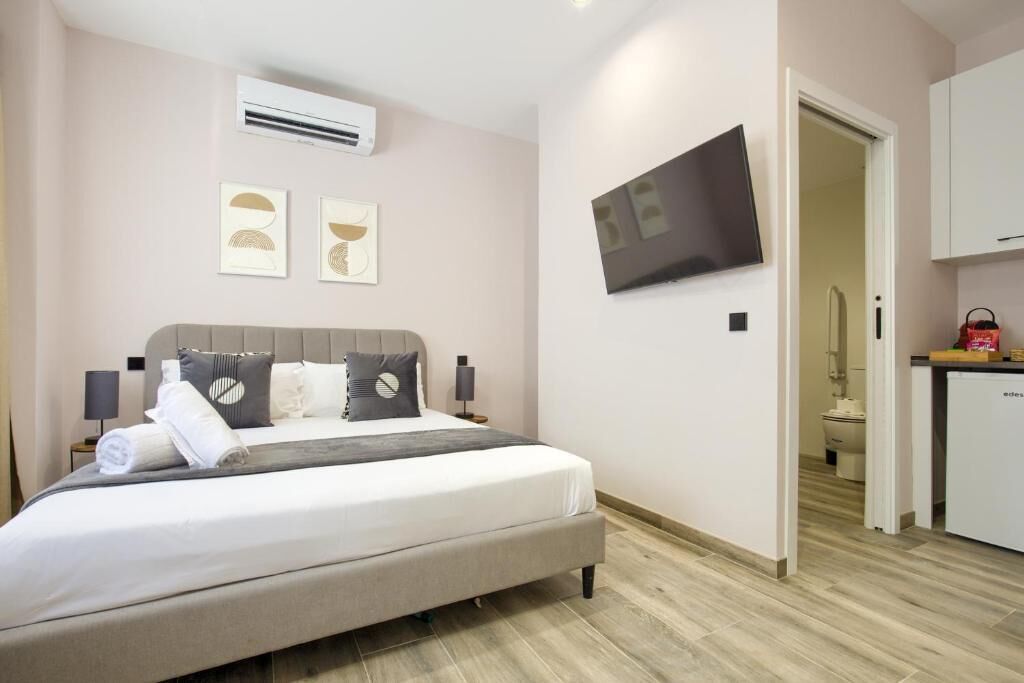 Quarto com cama, mesas de cabeceira, televisão de tela plana e uma cozinha compacta.