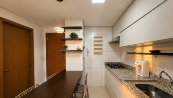 Cozinha moderna com armários brancos, bancada de granito, forno embutido e pia de aço inoxidável.