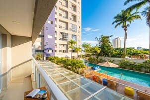 Varanda com guarda-corpo de vidro com vista para uma piscina e o horizonte urbano.