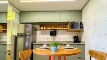 Cozinha moderna com micro-ondas embutido, cafeteira e mesa de jantar com cadeiras.