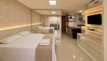 Quarto de hotel moderno com uma cama grande, televisão, secretária e varanda com vista para a cidade.