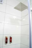 Casa de banho moderna com azulejos brancos, um chuveiro e dois dispensadores de produtos de higiene pessoal vermelhos.