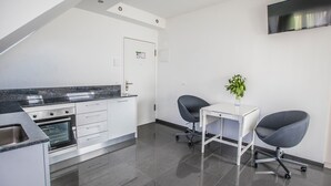 Cozinha moderna com forno embutido, área de jantar com duas cadeiras e uma mesa branca.