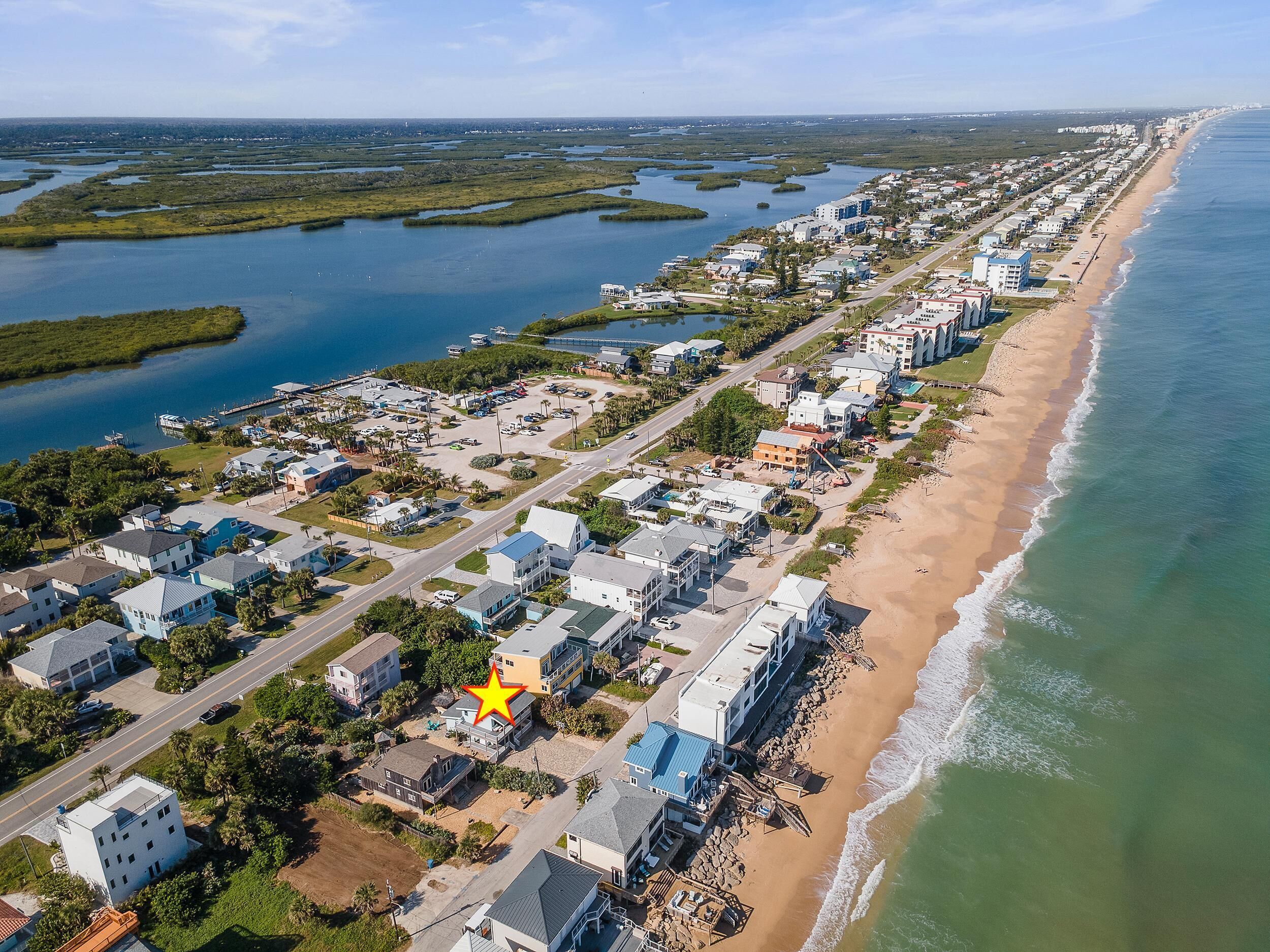 Vista aérea de uma área residencial costeira com casas, praia e corpos d'água.