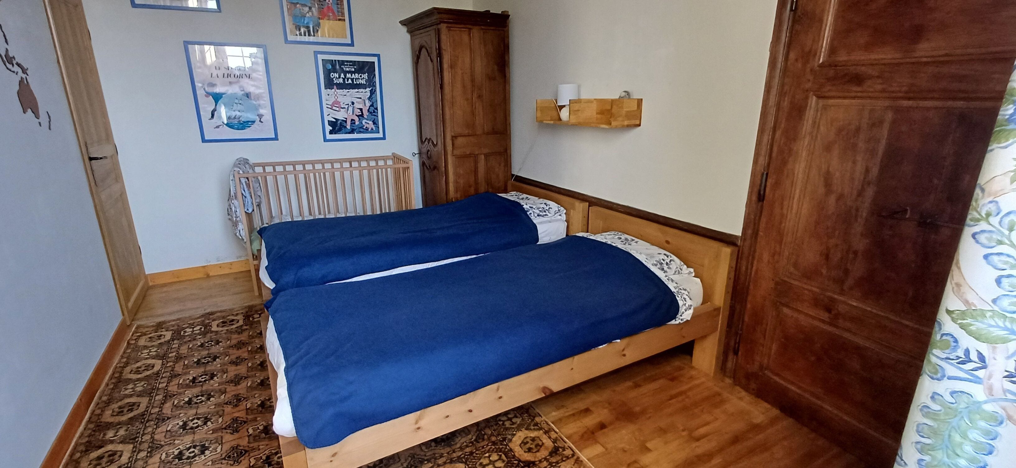 Um quarto pequeno com duas camas de solteiro, um guarda-roupa de madeira, um radiador e uma parede decorada com quadros.