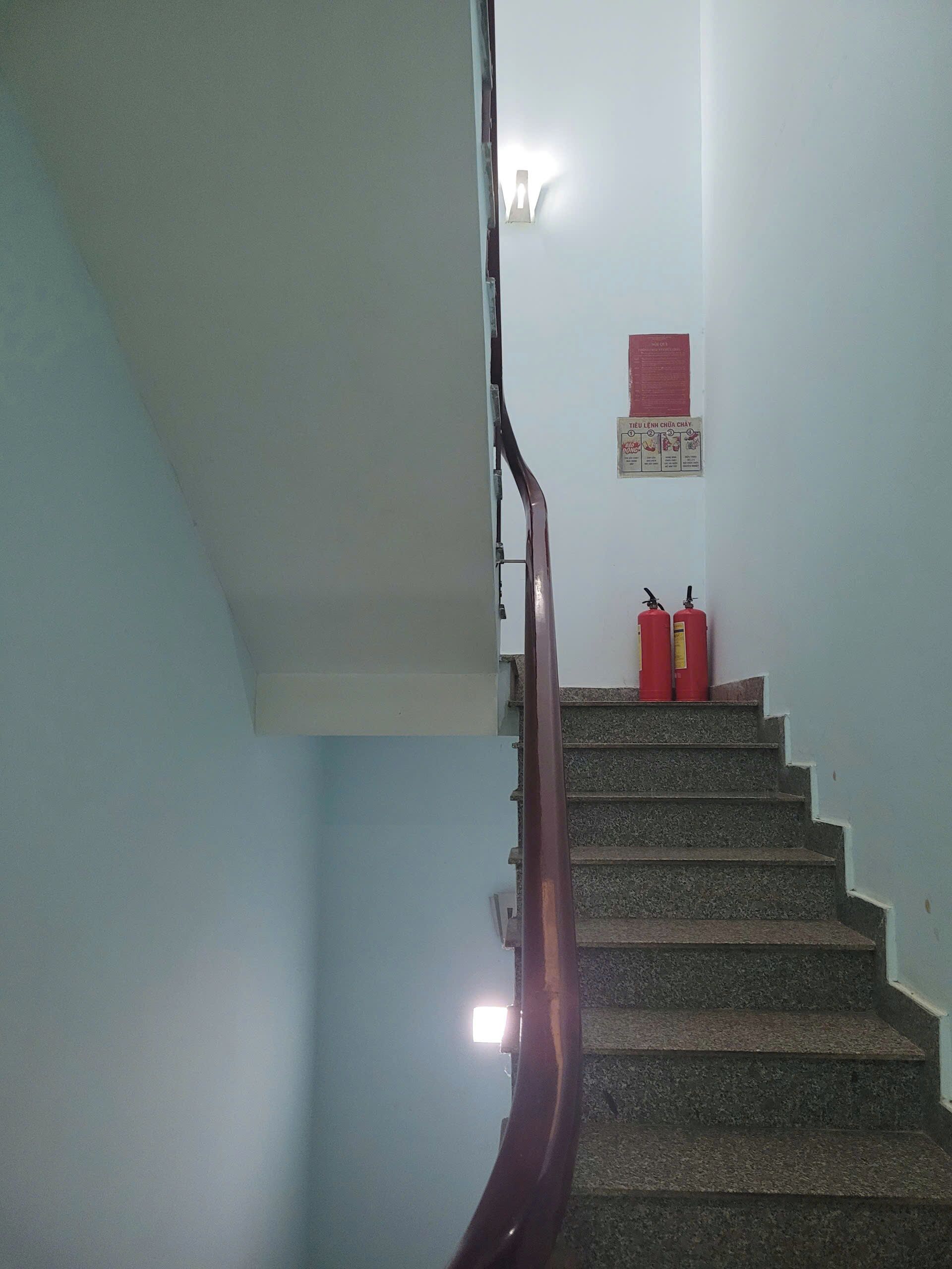 Uma escadaria com corrimão, um extintor de incêndio e uma placa de segurança na parede.