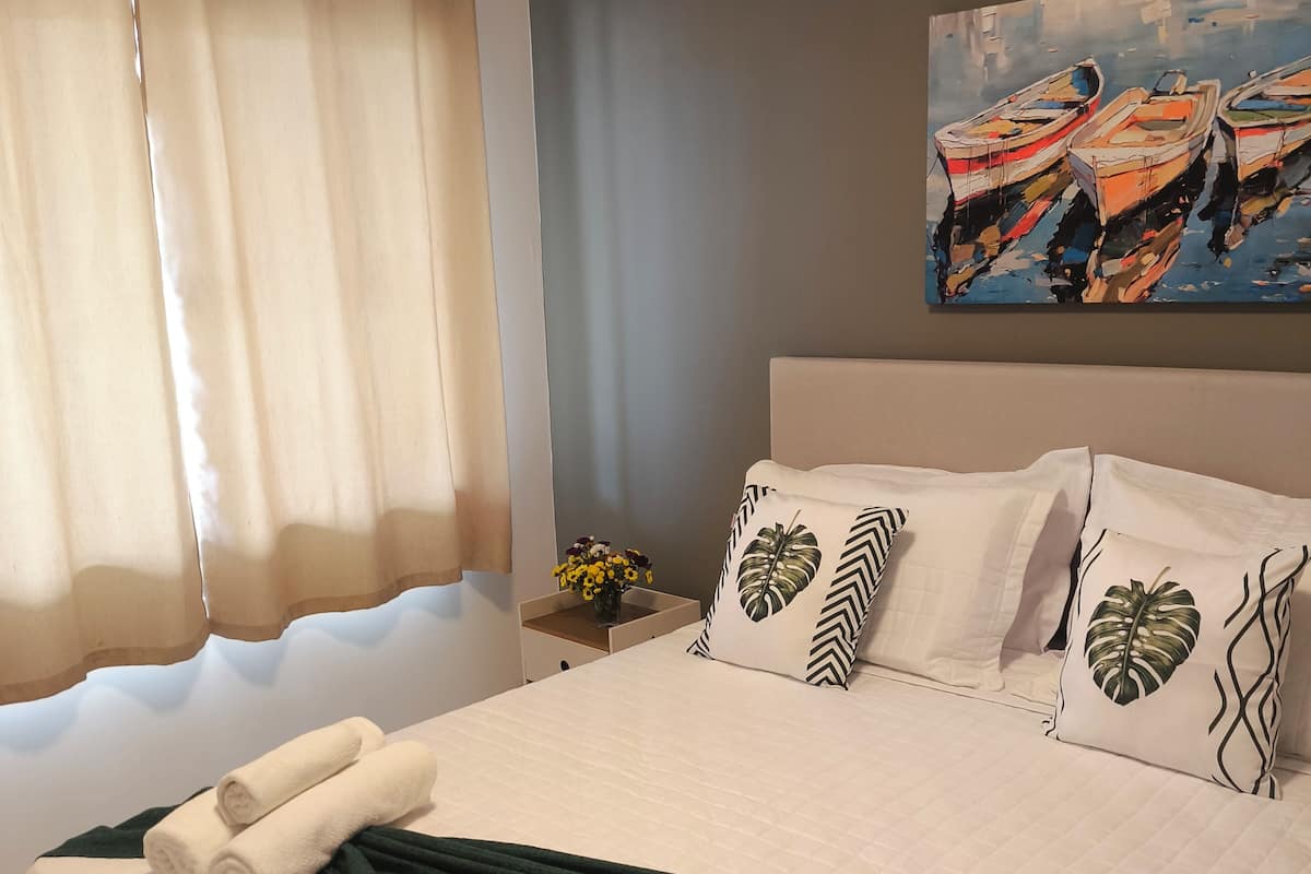 Cama bem arrumada com manta verde, roupa de cama branca e almofadas decorativas com estampas de folhas.