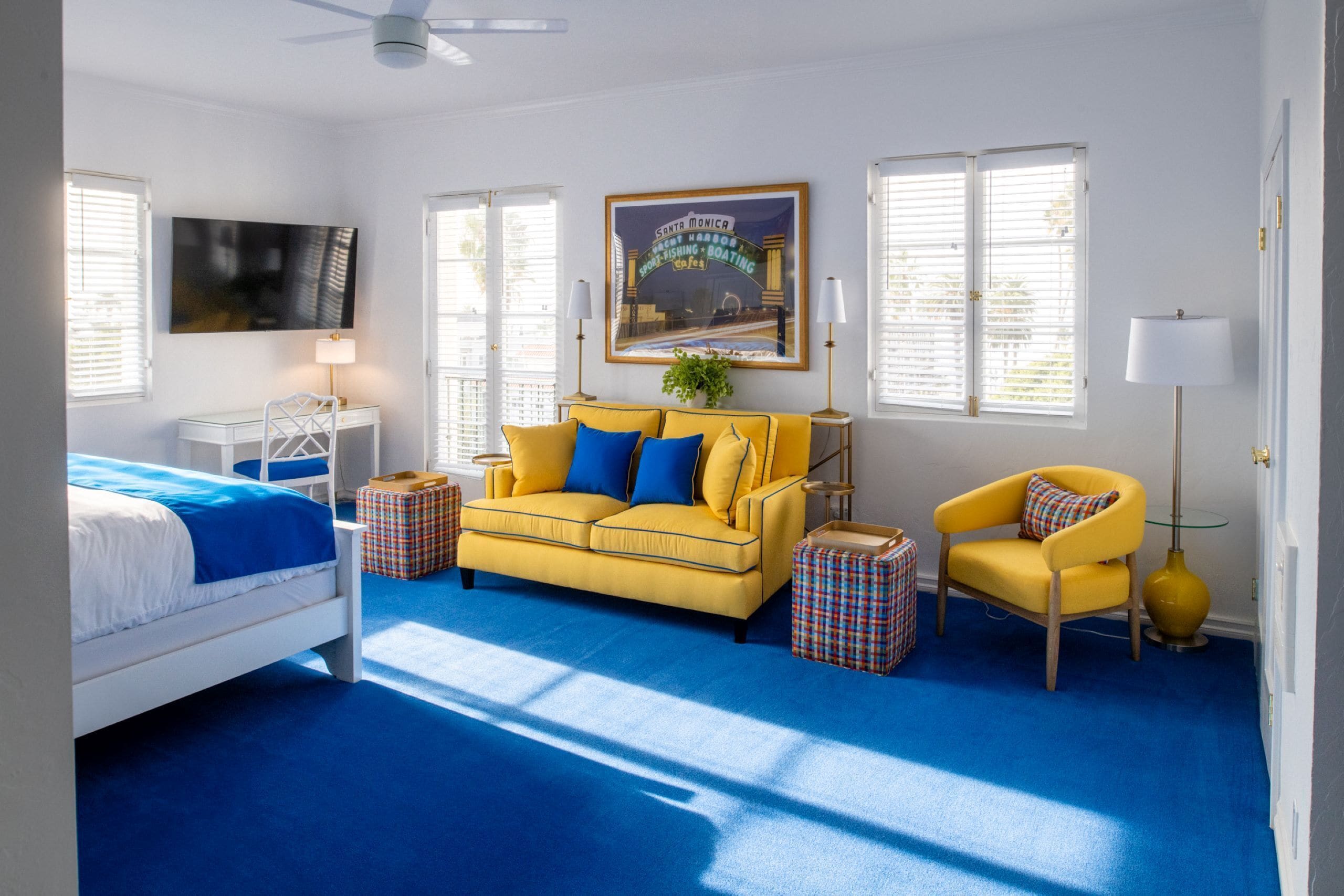 Quarto com cama, sofá amarelo, poltrona amarela, mesa pequena e luminária de chão.