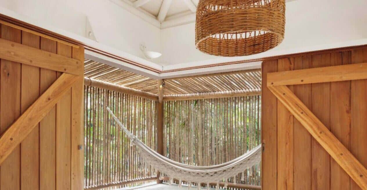 Uma rede pendurada entre vigas de madeira em um quarto com teto alto e uma cesta de palha suspensa.