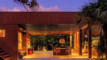 Um edifício moderno com área externa coberta, degraus que levam a um espaço de estar e vista para a paisagem ao redor.