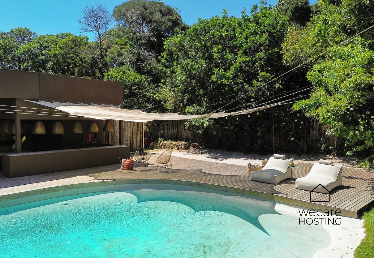 Piscina com espreguiçadeiras, deck de madeira e área de estar coberta.