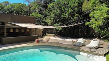 Piscina com espreguiçadeiras, deck de madeira e área de estar coberta.