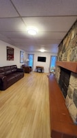 Uma sala de estar espaçosa, com piso de madeira, sofá de couro marrom, lareira de pedra e televisão de tela plana na parede.