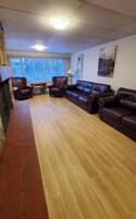 Uma sala de estar espaçosa com piso de madeira, um amplo sofá e uma lareira.