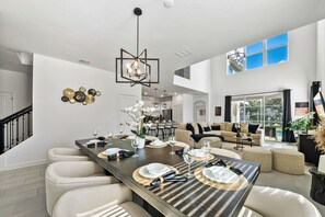 Uma sala de estar ampla, com uma grande mesa de jantar, assentos confortáveis e um lustre moderno.