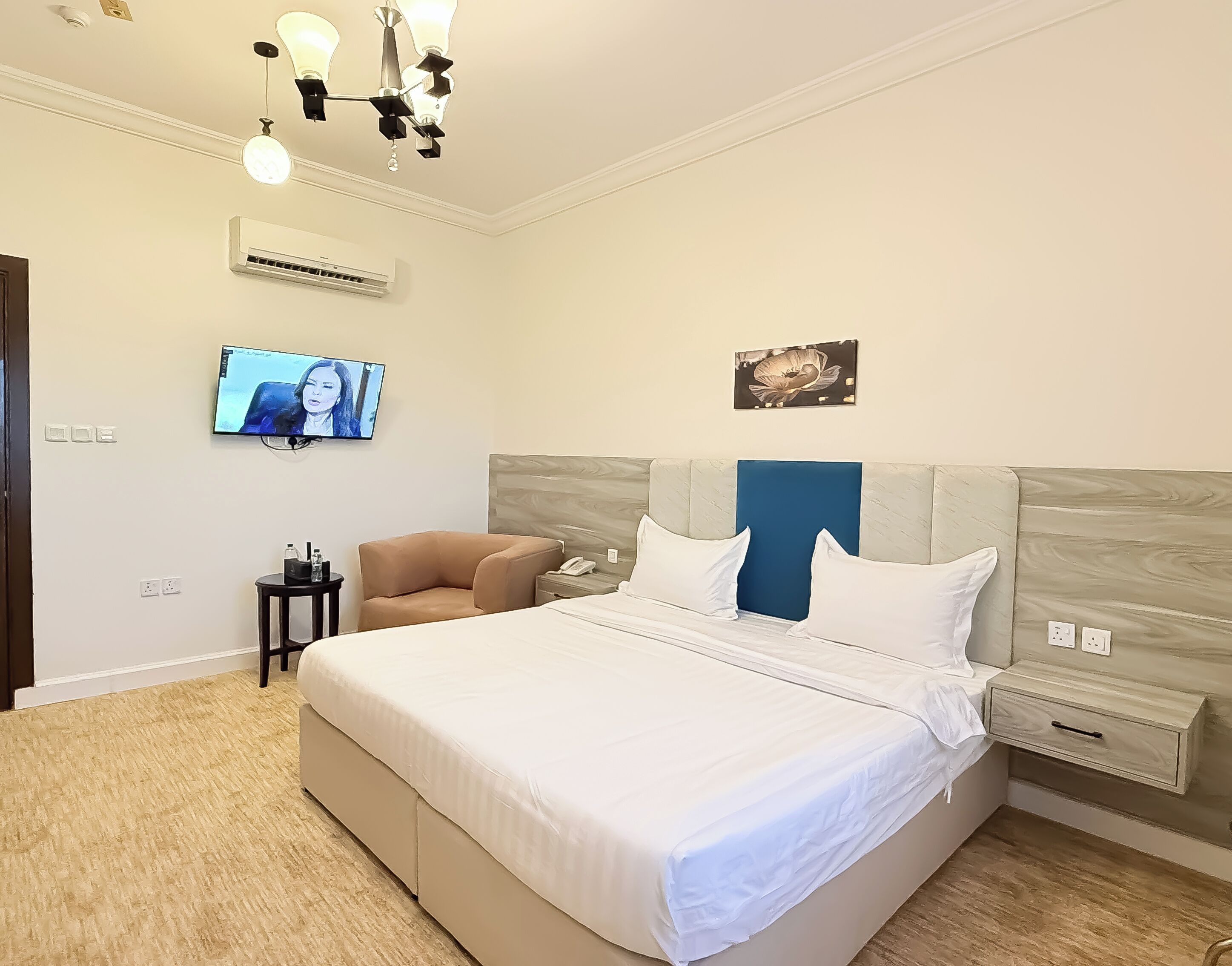 Quarto de hotel com uma cama grande, televisão fixada na parede, mesa de cabeceira com abajur e unidade de ar condicionado.