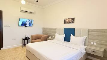 Quarto de hotel com uma cama grande, televisão fixada na parede, mesa de cabeceira com abajur e unidade de ar condicionado.