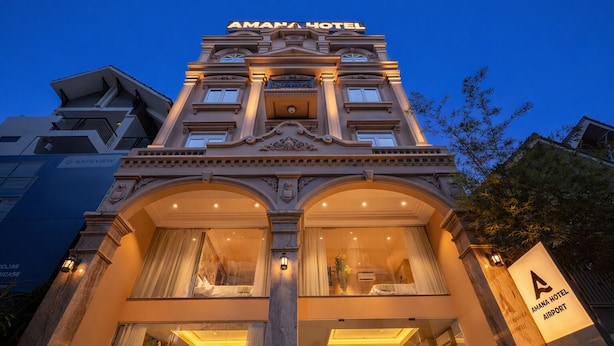 Um hotel com arquitetura clássica, apresentando uma entrada destacada com duas arcos e uma placa com a inscrição 'AMANA HOTEL'.