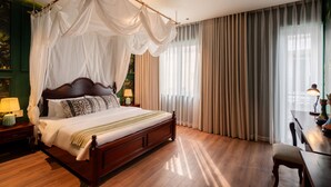 Um quarto espaçoso com uma cama grande, piso de madeira, dossel e vista para o exterior através de amplas janelas.