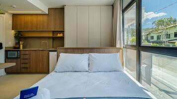Quarto de hotel moderno com uma cama, pequeno espaço de cozinha e uma grande janela com vista para o exterior.