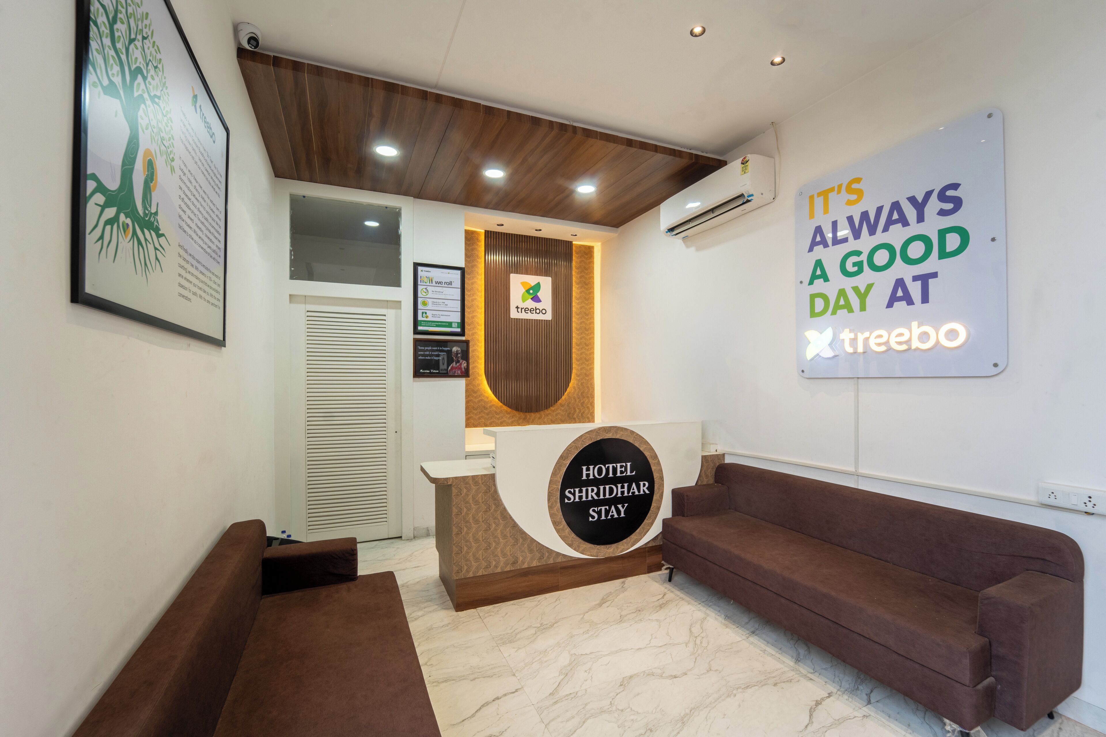 Uma área de recepção de hotel com um balcão de madeira, um sofá marrom e uma placa que diz 'It's always a good day at treebo'.