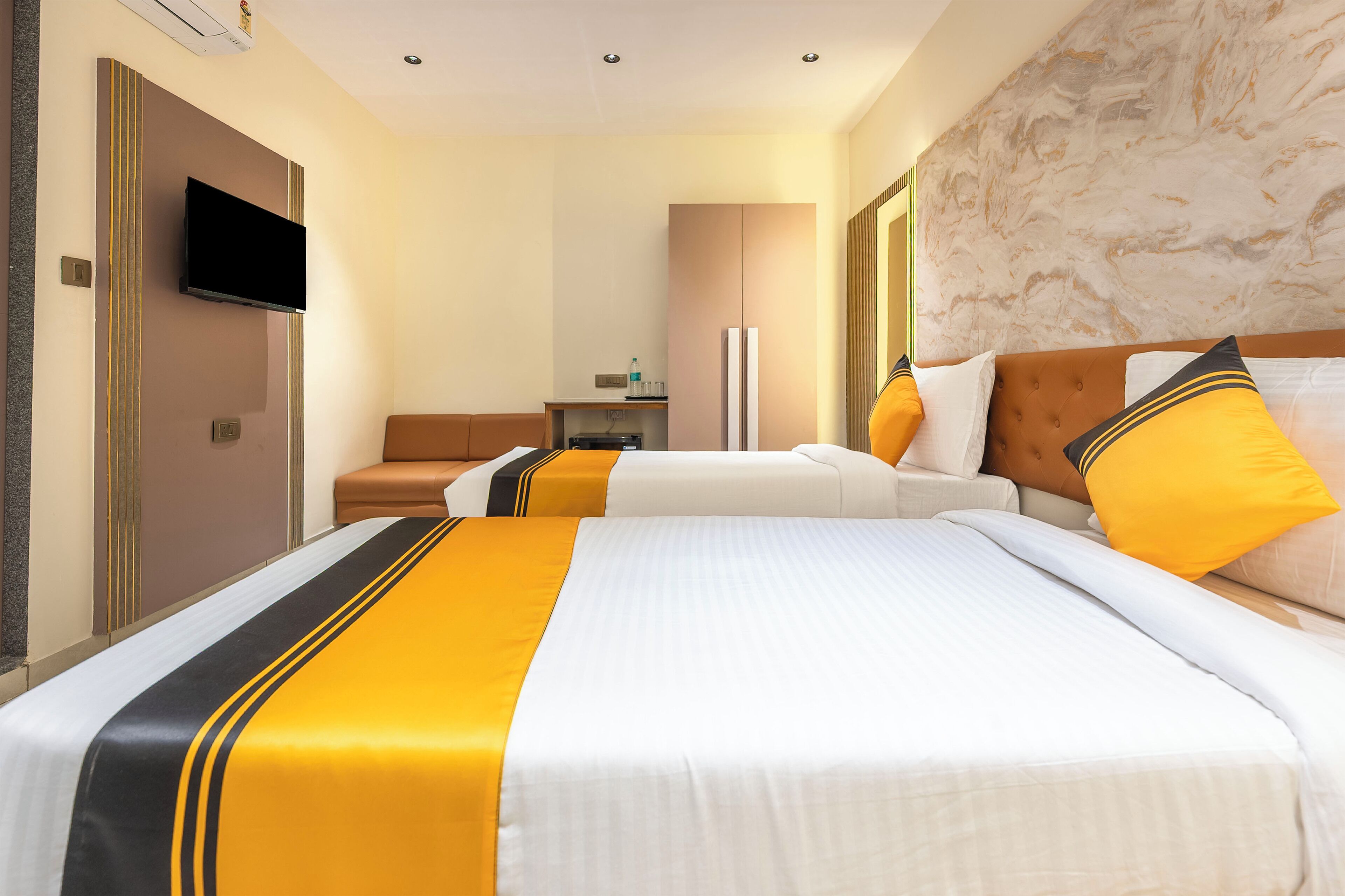 Quarto de hotel com duas camas, televisão, minibar e parede de mármore.