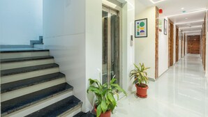 Um saguão de hotel moderno com escada, plantas em vasos e um longo corredor que leva à área de recepção.